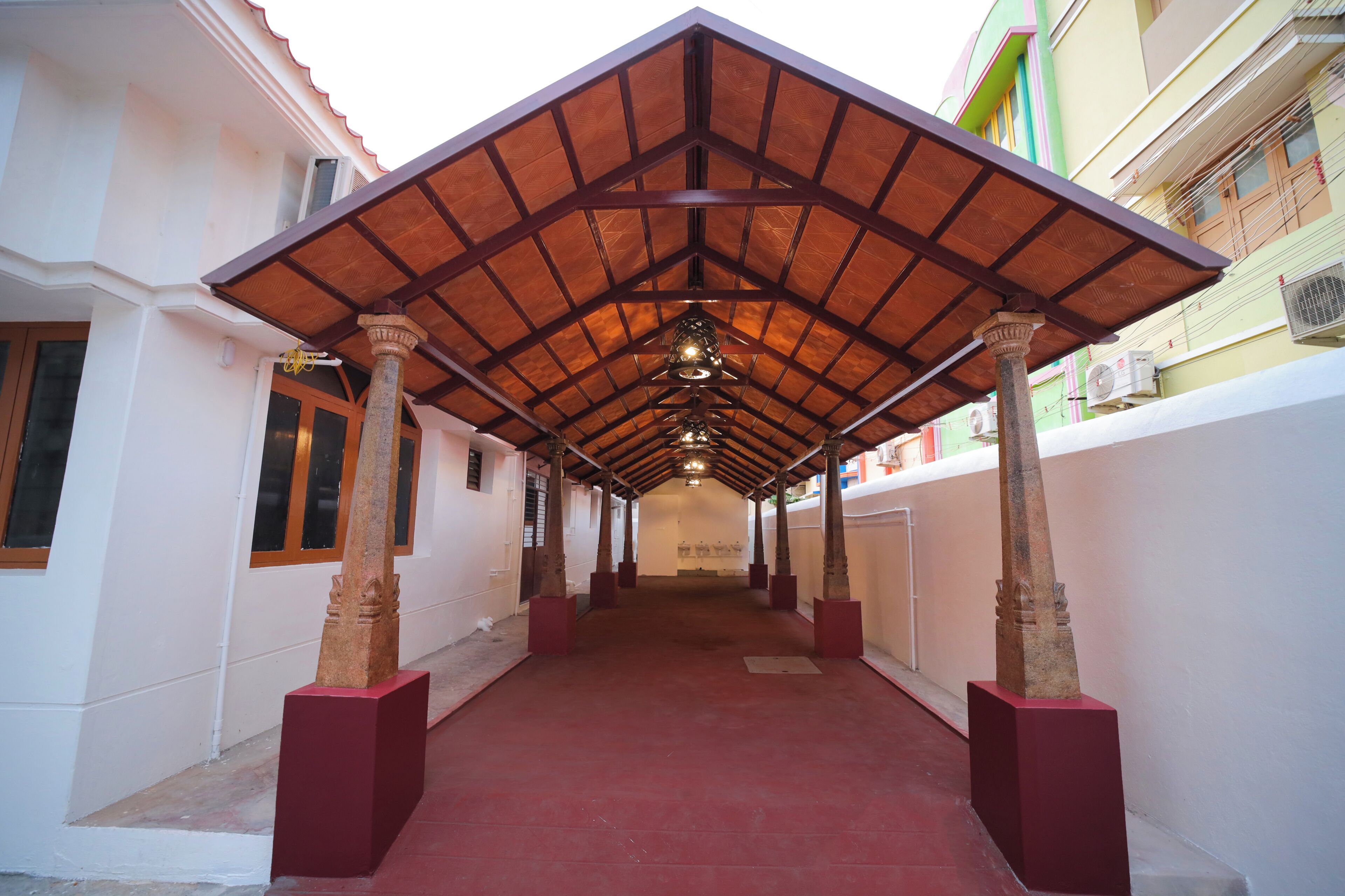 Uma galeria coberta com piso vermelho, sustentada por colunas, leva a uma entrada de edifício.