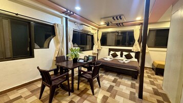 Quarto com cama, mesa e cadeiras, planta em vaso e janela com cortinas.