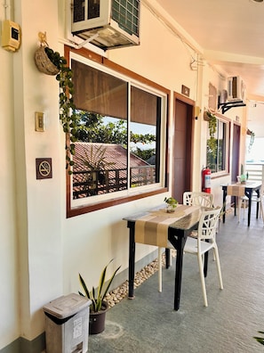 Uma área de estar externa limpa e bem cuidada, com mesa, cadeiras, lixeira e um vaso de planta.