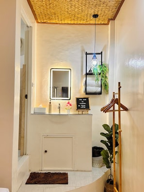 Uma área de recepção com espelho, placa de boas-vindas, luminária pendente e porta-casacos.