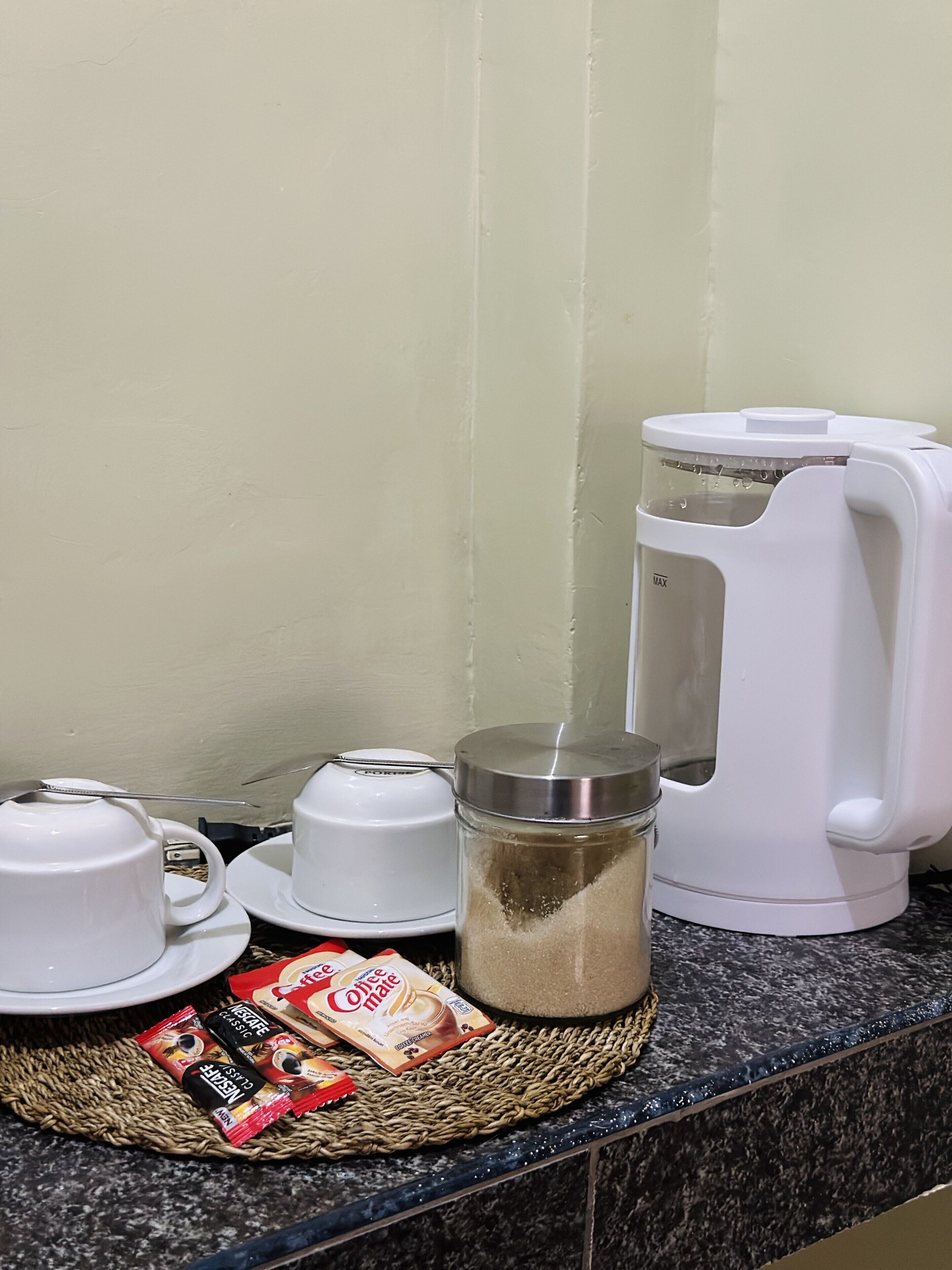 Uma bancada de cozinha com uma cafeteira, um pote de açúcar e sachês de café instantâneo.