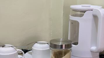 Uma bancada de cozinha com uma cafeteira, um pote de açúcar e sachês de café instantâneo.