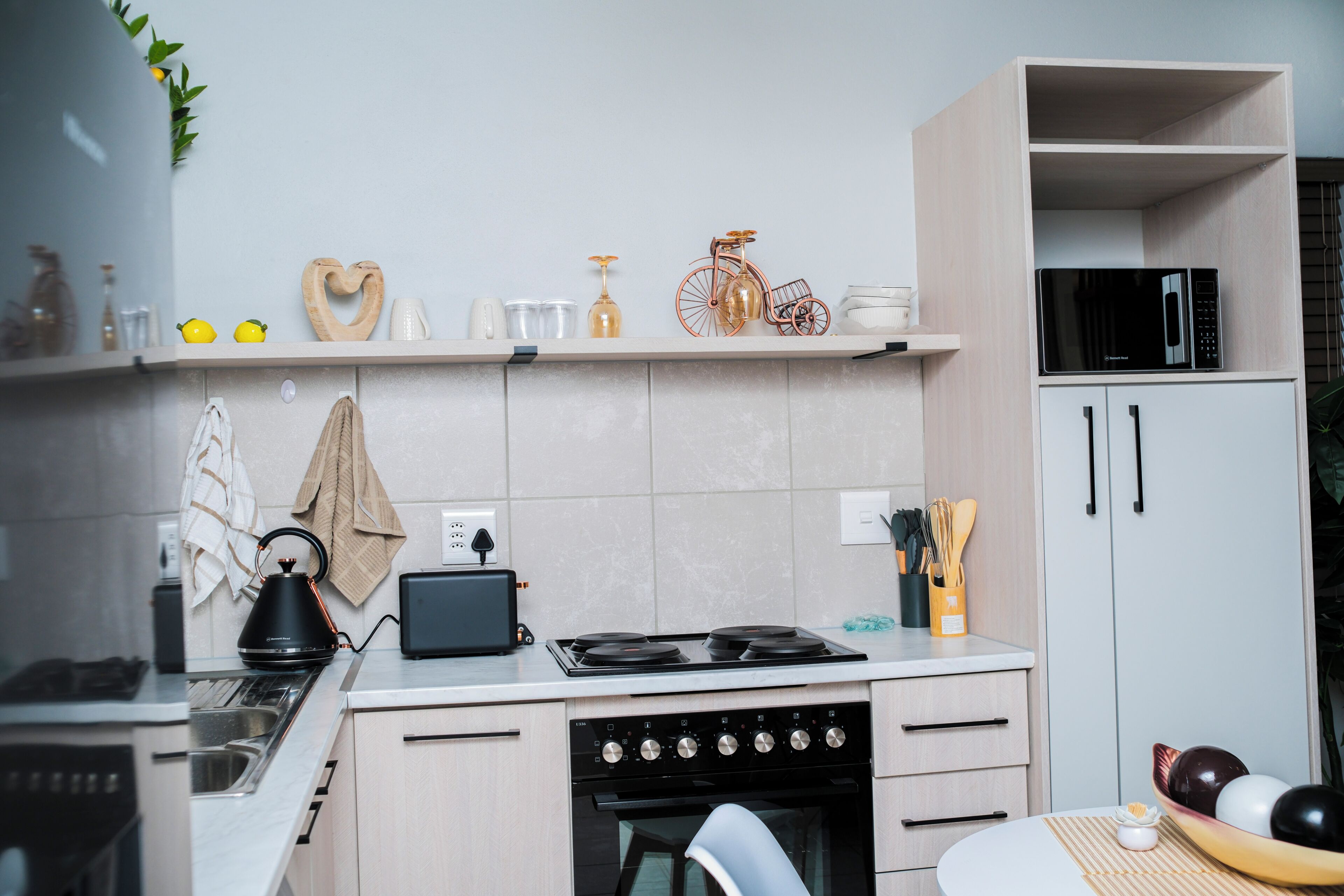 Cozinha moderna com fogão, forno e micro-ondas. Há prateleiras com utensílios de cozinha e uma bicicleta decorativa.
