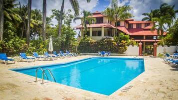 Piscina com água azul, cercada por espreguiçadeiras e palmeiras.
