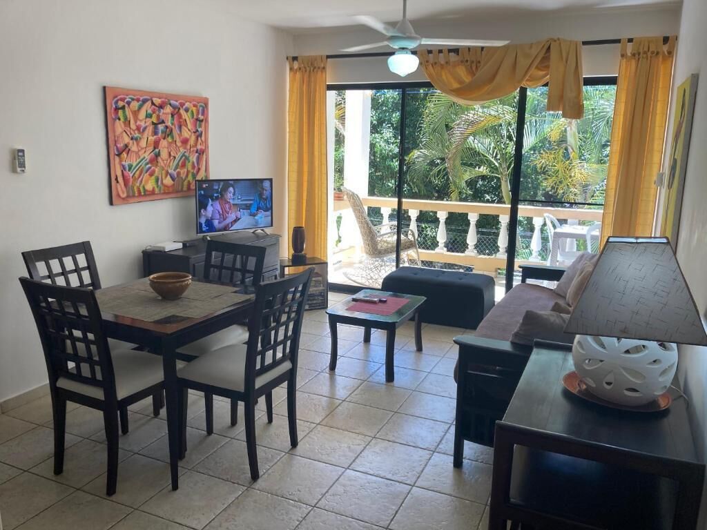 Sala de estar com área de jantar, televisão e varanda com vista para o verde.
