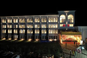 Um edifício de vários andares com uma fileira de janelas em arco e um palco com pessoas reunidas.