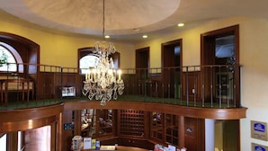 Interior de um hotel com vários níveis, um lustre imponente, varandas de madeira e vista para o exterior.