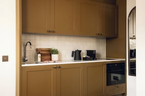 Cozinha com armários marrons, pia de aço inoxidável, cafeteira e forno preto.