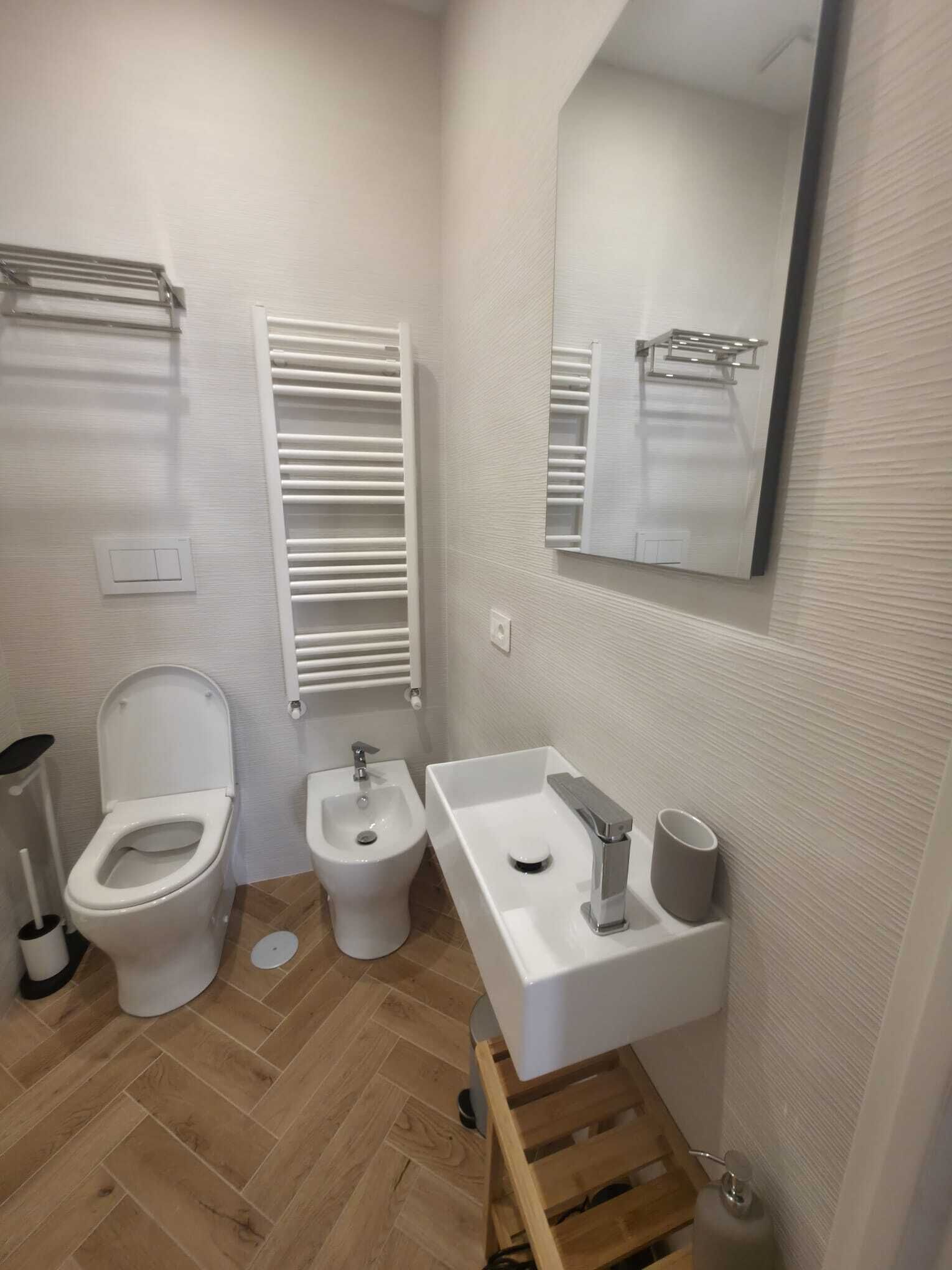 Casa de banho com sanita, bidé, lavatório e suportes para toalhas.
