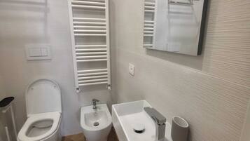 Casa de banho com sanita, bidé, lavatório e suportes para toalhas.