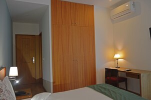 Quarto de hotel com cama, escrivaninha, cadeira, guarda-roupa e ar condicionado.