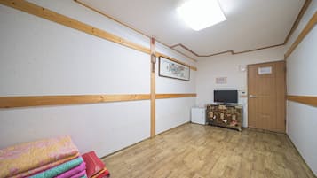Quarto com vigas de madeira no teto, televisão, armário com painel decorativo e uma pilha de toalhas dobradas.