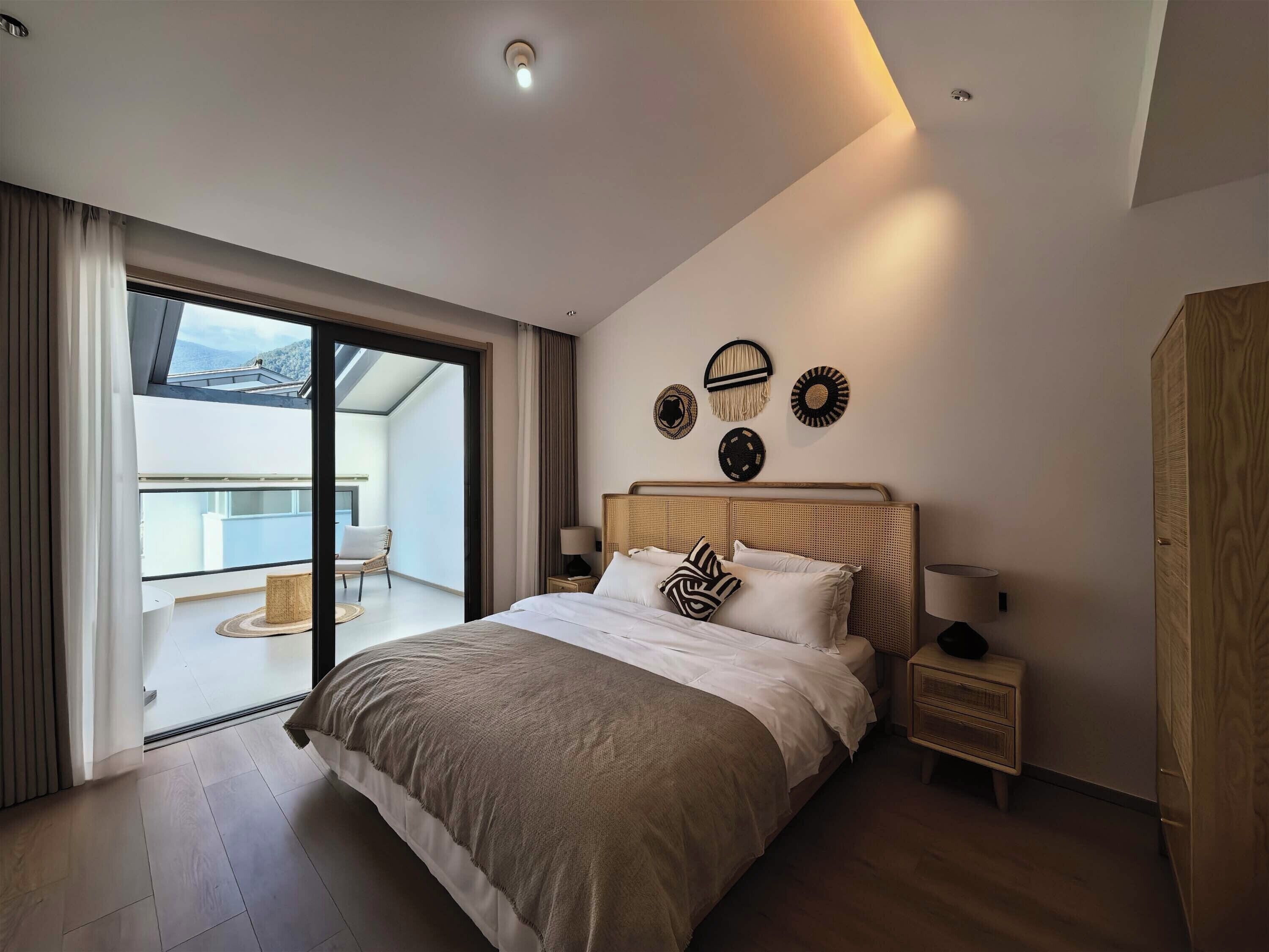 Quarto moderno com cama grande, varanda e vista, e guarda-roupa de madeira.