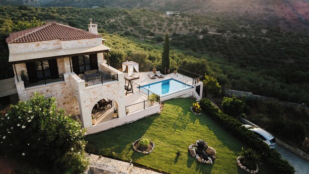 Uma villa com piscina, um pátio com móveis de exterior e vista para as colinas circundantes.