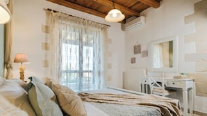 Quarto com cama, escrivaninha, cadeira e janela com cortinas.