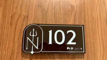 Uma placa preta e branca com o número '102' e a palavra 'PARSHWA' numa superfície de madeira.