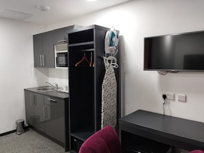 Quarto de hotel compacto com cozinha compacta, televisão de tela plana e guarda-roupa com cabideiro.