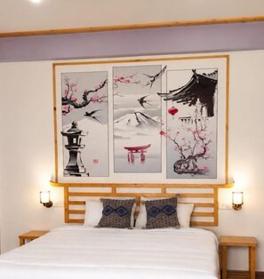 Quarto com cama, cabeceira de madeira e obra de arte na parede retratando flores de cerejeira e arquitetura tradicional.