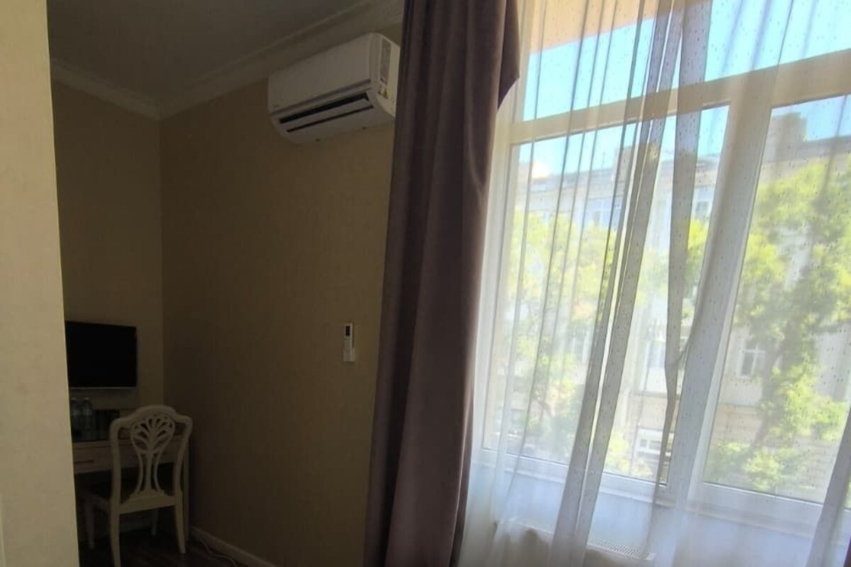 Quarto de hotel com cama, escrivaninha, cadeira e janela com cortinas.