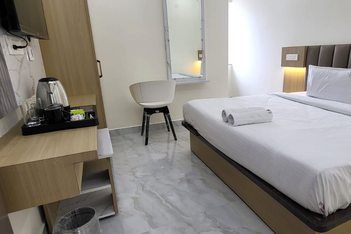 Quarto de hotel com cama, uma cadeira, escrivaninha e espelho.