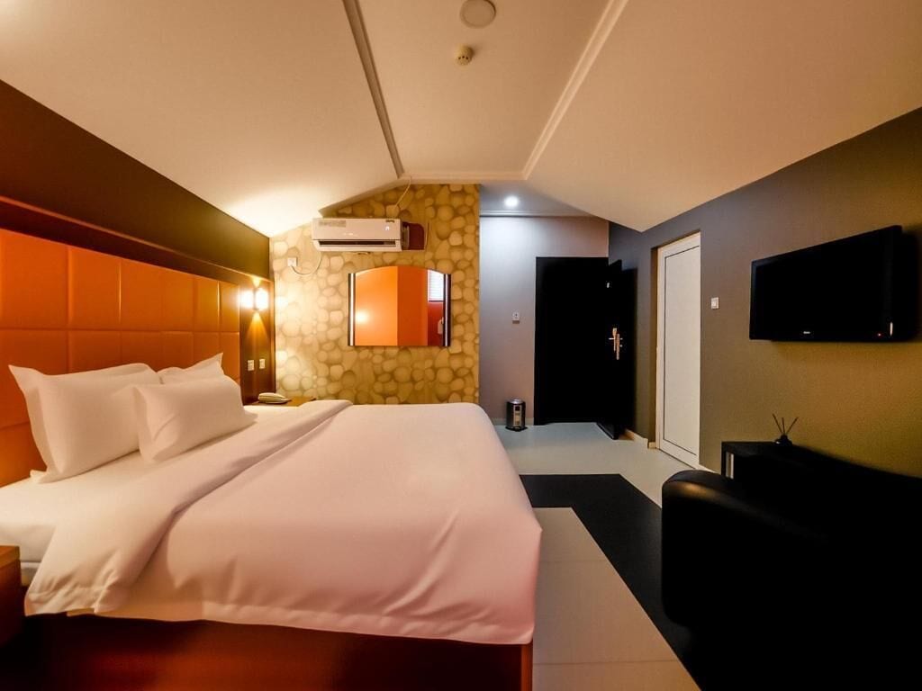 Quarto de hotel com uma cama, televisão e parede de pedra.