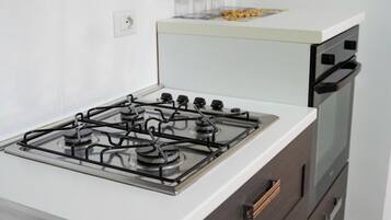 Cozinha com fogão a gás, forno e bancada branca.