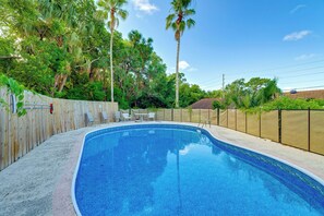 Piscina com deck de madeira, cercada por um muro de madeira e vegetação exuberante.