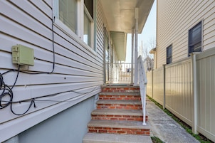 Fachada residencial com escadaria de tijolos que leva a um alpendre, parede externa branca e cerca.