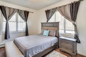 Quarto com cama, mesa de cabeceira e cortinas.