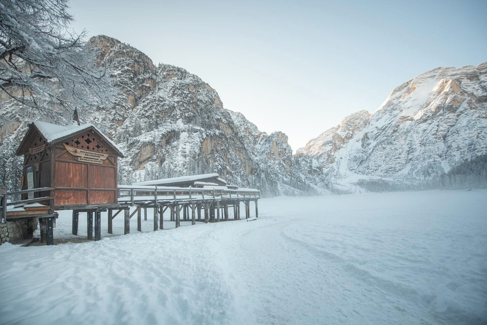 Uma cabana de madeira com uma placa, um cais de madeira e montanhas cobertas de neve ao fundo.