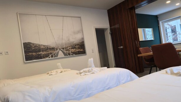 Quarto de hotel com duas camas, uma escrivaninha e uma cadeira.
