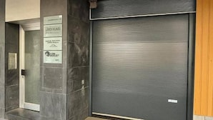 Entrada de um edifício com uma porta de metal fechada e uma placa na parede.