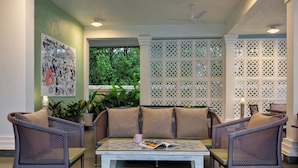 Uma área de estar com móveis de vime e uma mesa de centro branca, cercada por uma treliça decorativa branca.