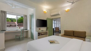 Quarto de hotel com cama, escrivaninha, cadeira, televisão e sofá.