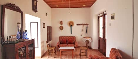 Quarto com teto de madeira, sofá, mesa, cadeiras, espelho e porta-chapéus fixado na parede.