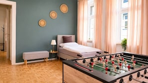 Quarto com cama, mesa de pebolim, um banco e uma mesinha de cabeceira com abajur.
