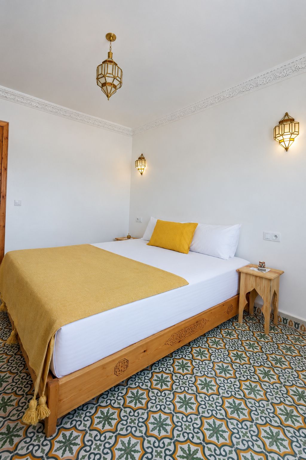Quarto com cama, duas luzes na parede e piso com ladrilhos estampados.
