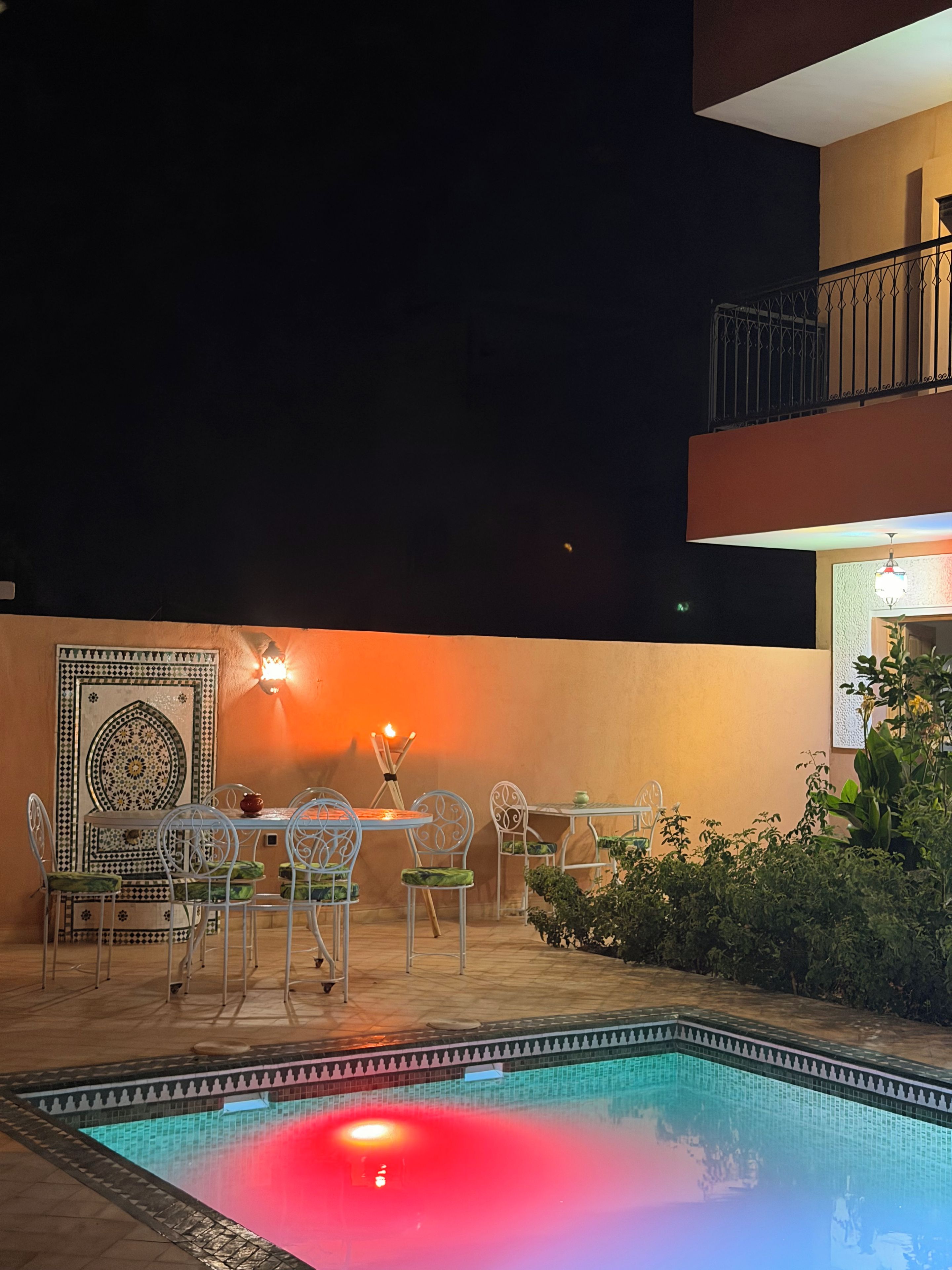 Área de piscina externa com espaço para refeições e um painel decorativo.