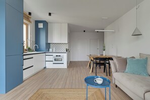 Cozinha moderna com armários brancos, sala de jantar com mesa e cadeiras de madeira e sala de estar com sofá e mesa de centro.