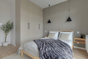 Quarto com cama, duas luminárias pendentes, mesa de cabeceira, planta em vaso e guarda-roupa.