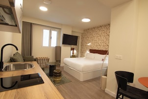 Quarto de hotel com cama, escrivaninha com pia, televisão e parede estampada.