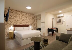 Quarto de hotel com cama, escrivaninha, cadeira, sofá e televisão.