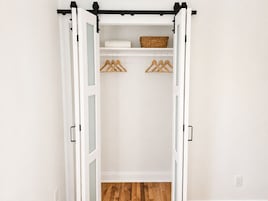 Um armário branco com porta de correr, cabides de madeira e uma cesta.