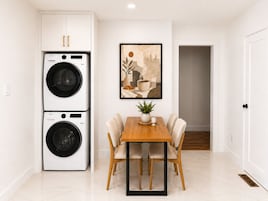 Cozinha moderna com máquina de lavar e secar integradas, mesa de jantar de madeira com cadeiras e uma obra de arte emoldurada na parede.
