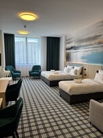 Quarto de hotel com piso xadrez, duas camas, escrivaninha, cadeiras e um quadro na parede.