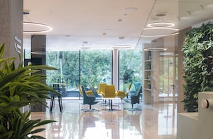Interior moderno com divisória de vidro, cadeiras amarelas e vista para o verde lá fora.