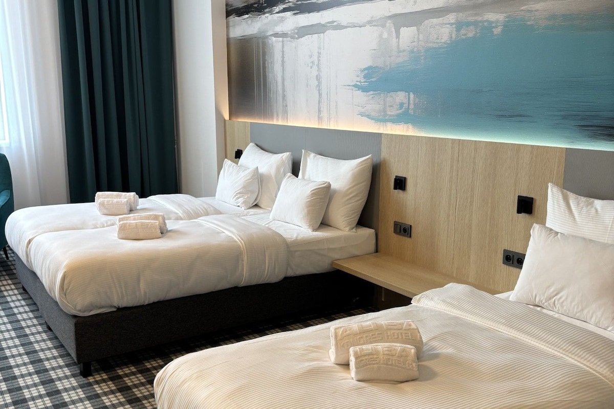 Quarto de hotel com duas camas, um quadro abstrato grande na parede e um chão xadrez.
