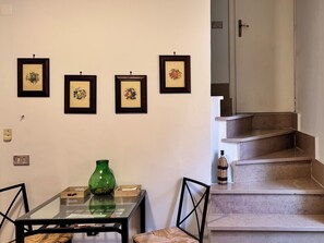 Um quarto com mesa de vidro, um vaso verde e quadros nas paredes.