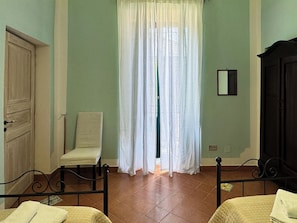 Quarto com cama, poltrona, guarda-roupa e janela com cortinas.