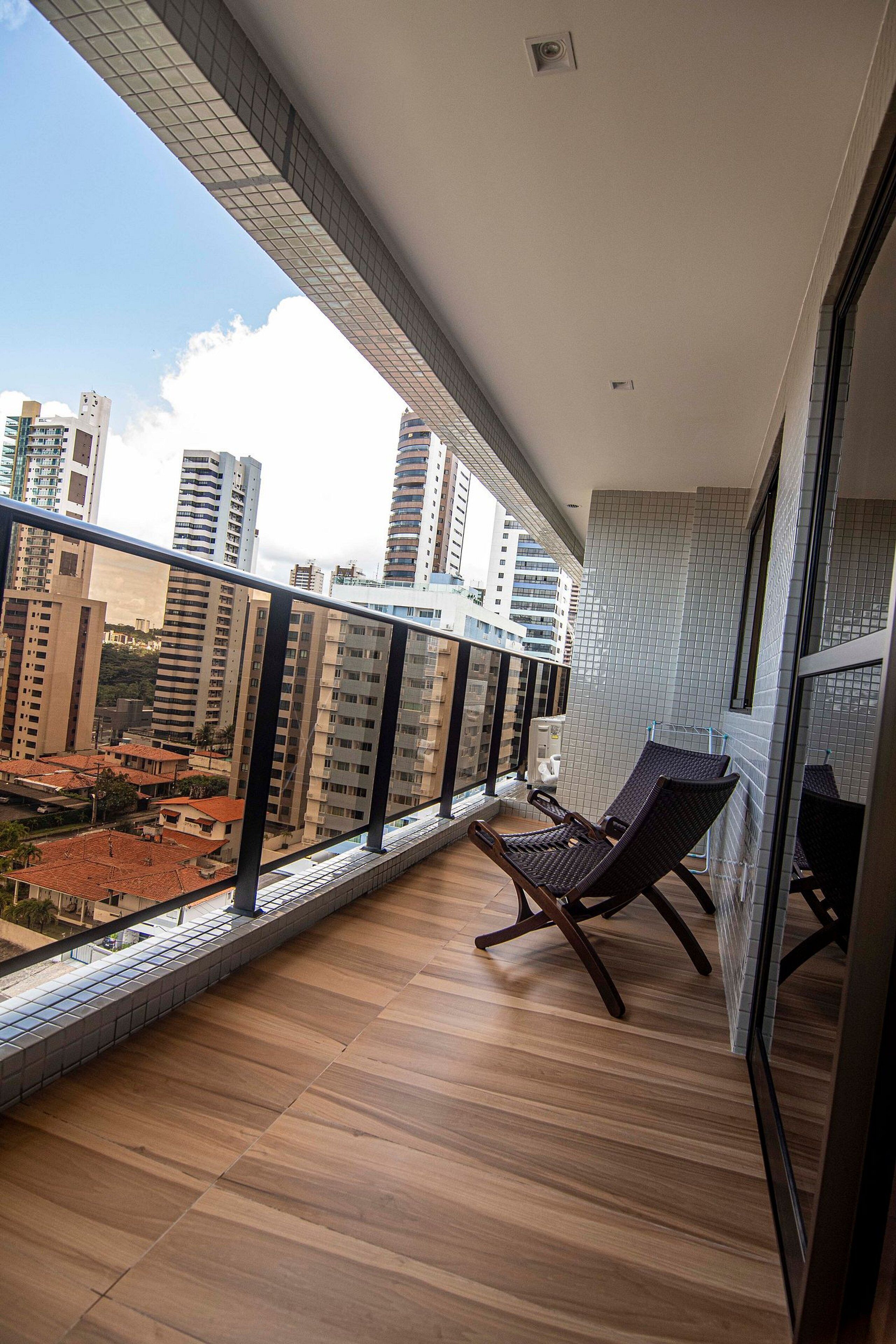 Varanda com vista para edifícios altos, piso de madeira e duas cadeiras de vime.